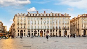 Uma grande praça pública com edifícios históricos, incluindo um banco e um café.