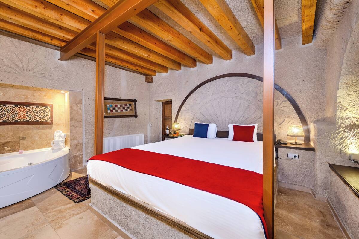 Quarto com uma cama grande, teto de madeira, parede de pedra, banheira e decoração de parede xadrez.