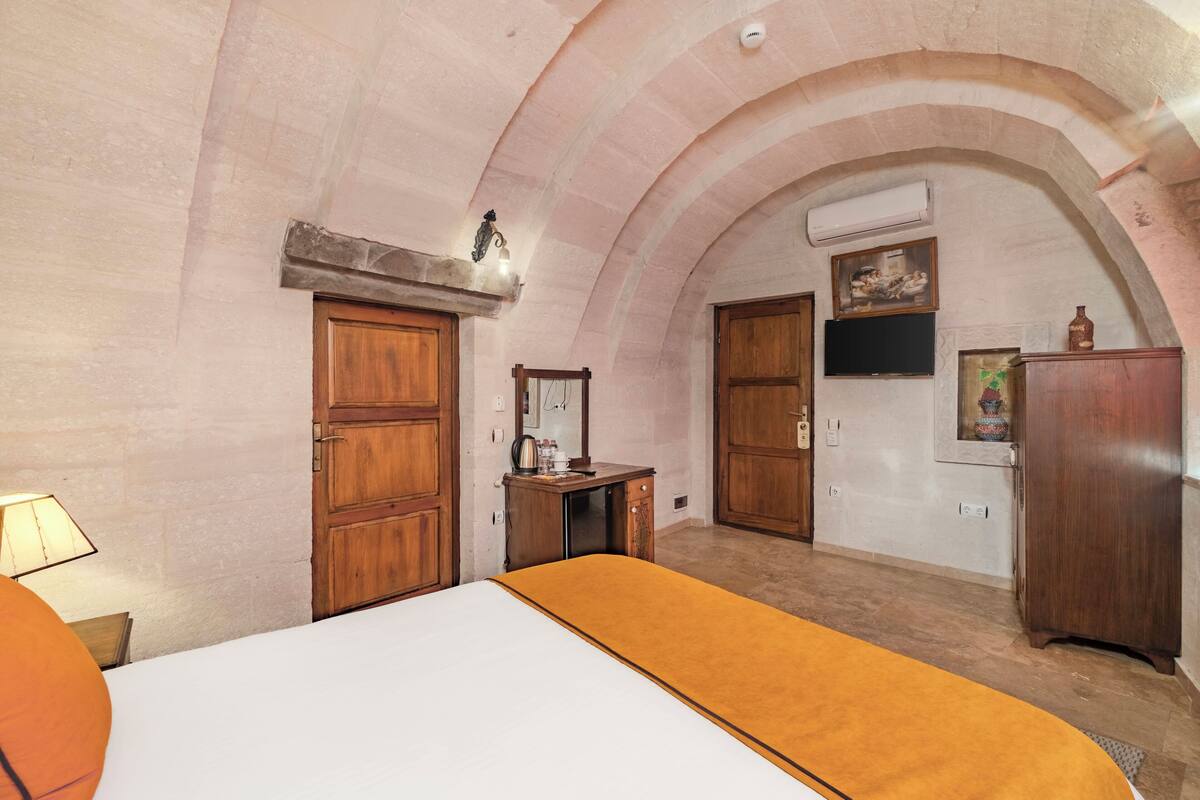 Quarto com cama, guarda-roupa de madeira, pequena escrivaninha com espelho e teto em arco.