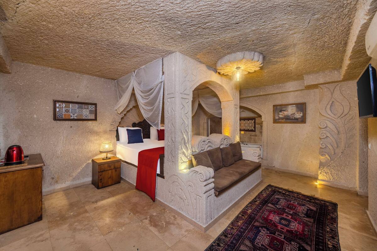 Um quarto com uma cama de dossel, um sofá, uma mesinha de centro com uma luminária e um tapete decorativo.
