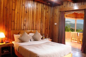 Quarto com painéis de madeira, uma cama, almofadas, uma mesa de cabeceira e vista para uma varanda.