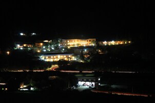 Um grande complexo de edifícios iluminado à noite, com vários níveis e área de estacionamento.