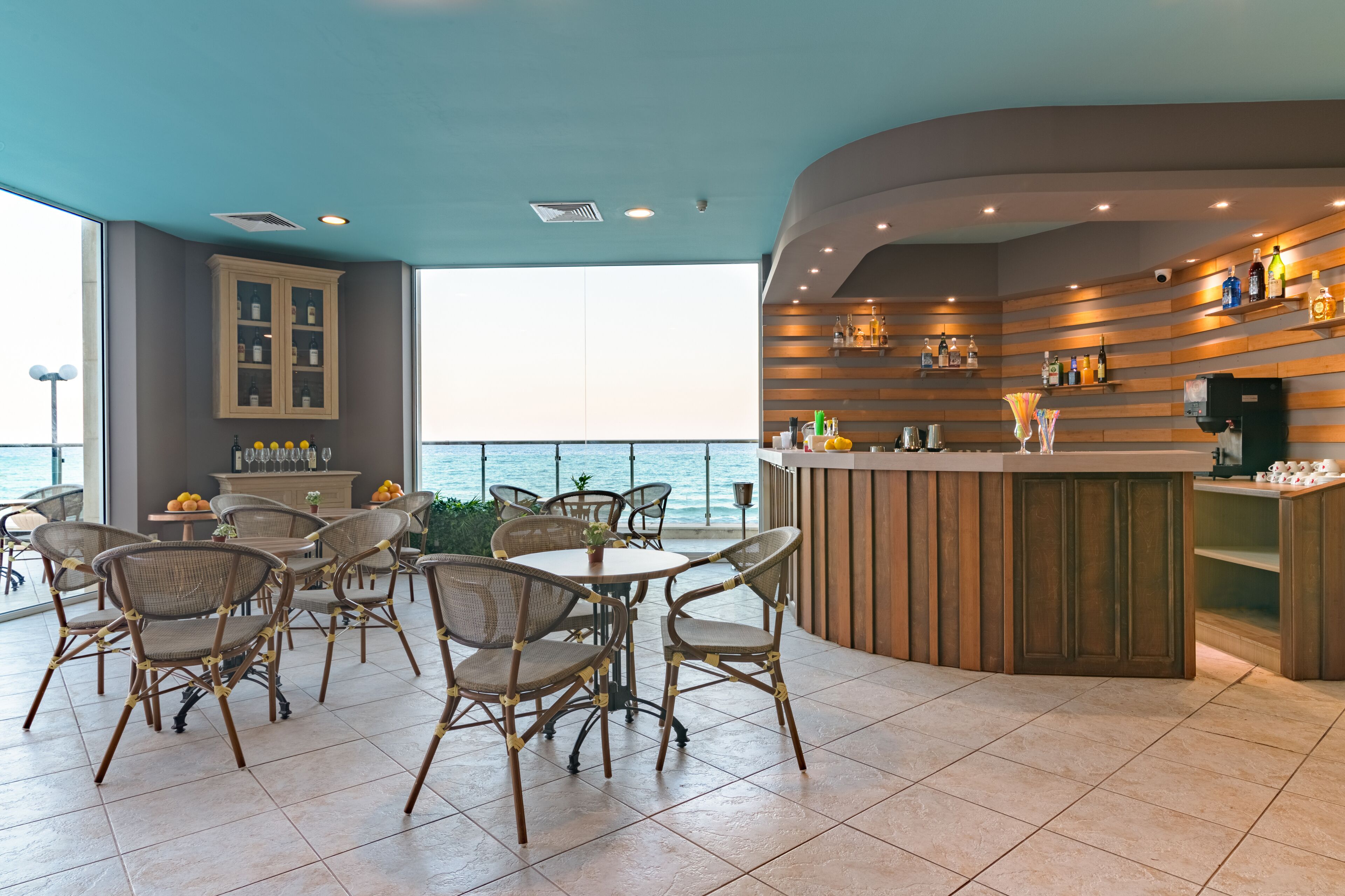 Uma área de bar moderna com balcão curvo, cadeiras de vime e vista para o mar.