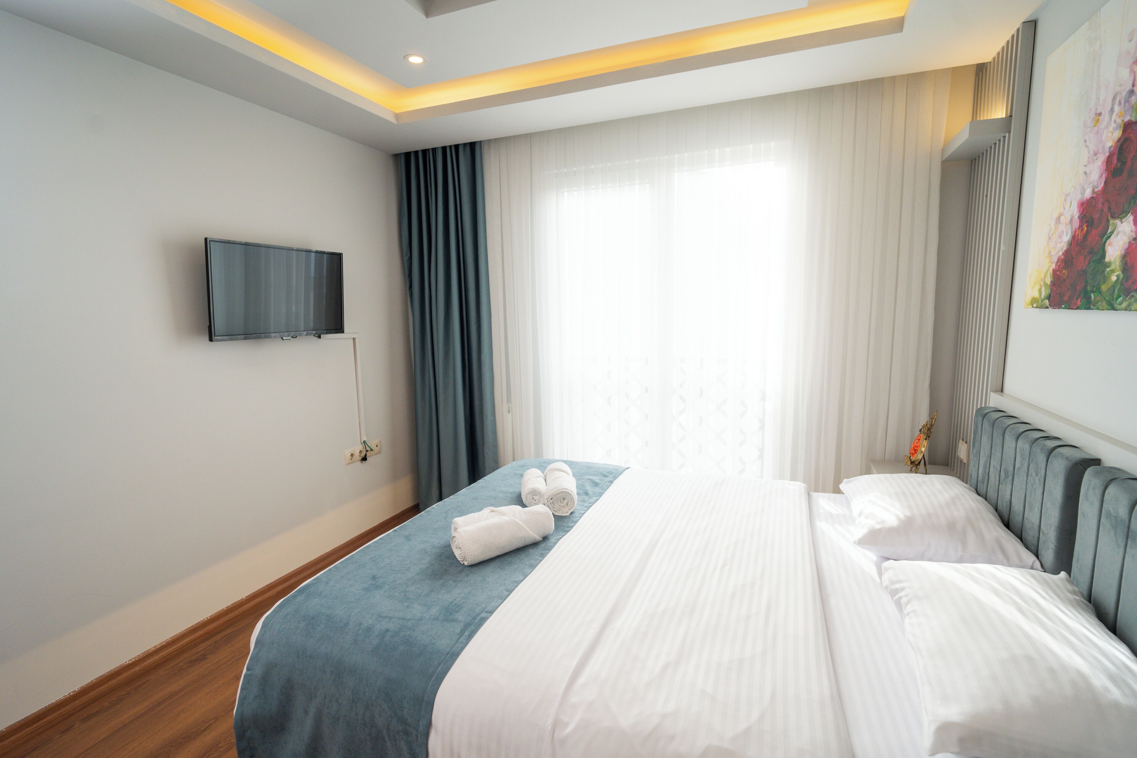 Quarto de hotel com cama, televisão de tela plana e uma janela grande com cortinas.