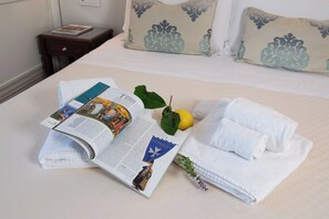 Cama bem arrumada com uma revista, um limão e toalhas dobradas.