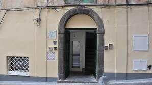 Entrada de um edifício com um arco, uma pequena janela com grade de metal e uma porta com painel de vidro.