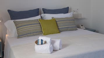 Cama bem arrumada com almofadas estampadas, telefone ao lado e toalhas dobradas sobre um lençol branco.