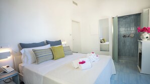 Quarto de hotel com cama, mesa de cabeceira com telefone, banheiro com chuveiro e espelho.