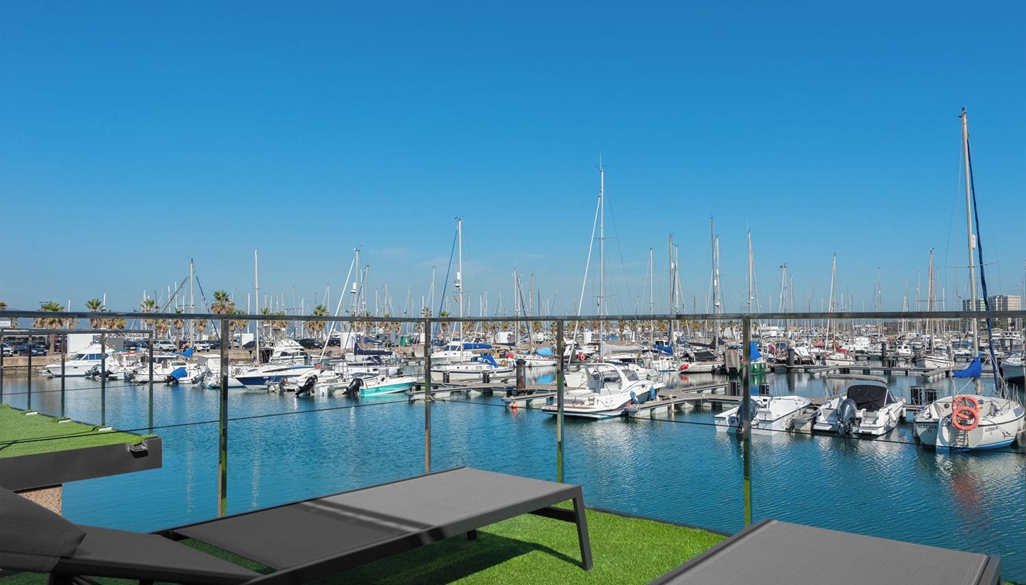 Uma marina com barcos atracados e cadeiras de sol em primeiro plano.