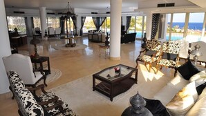 Ampla sala de estar com grande janela com vista para uma piscina, mobiliada com sofá, cadeiras e mesa de centro.
