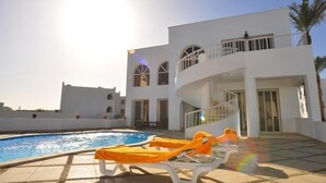 Um edifício moderno branco com piscina, espreguiçadeiras e uma palmeira.