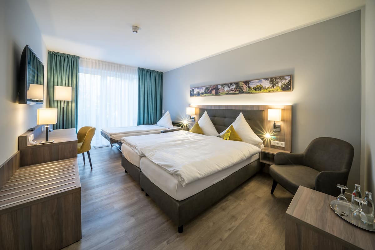 Quarto de hotel com uma cama grande, duas mesas de cabeceira, uma escrivaninha, uma cadeira e uma televisão.