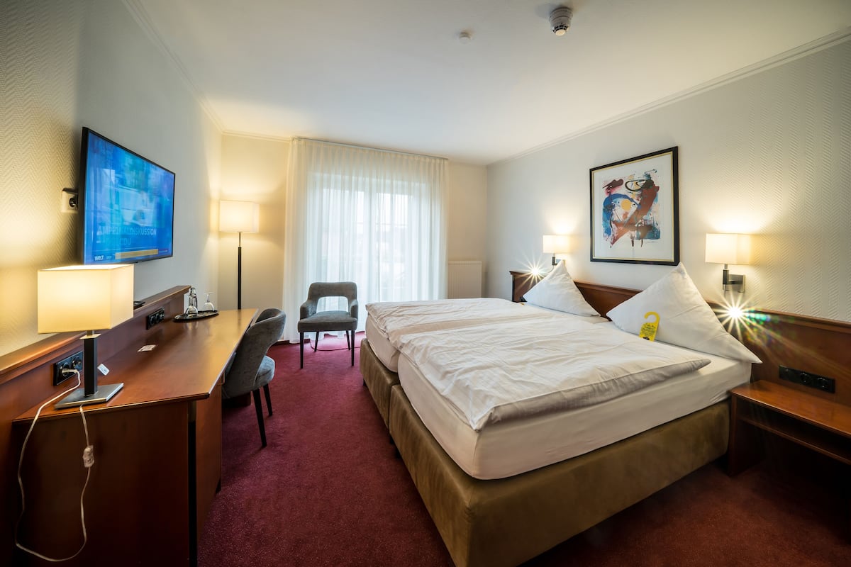 Quarto de hotel com uma cama grande, uma escrivaninha, uma cadeira e uma televisão.