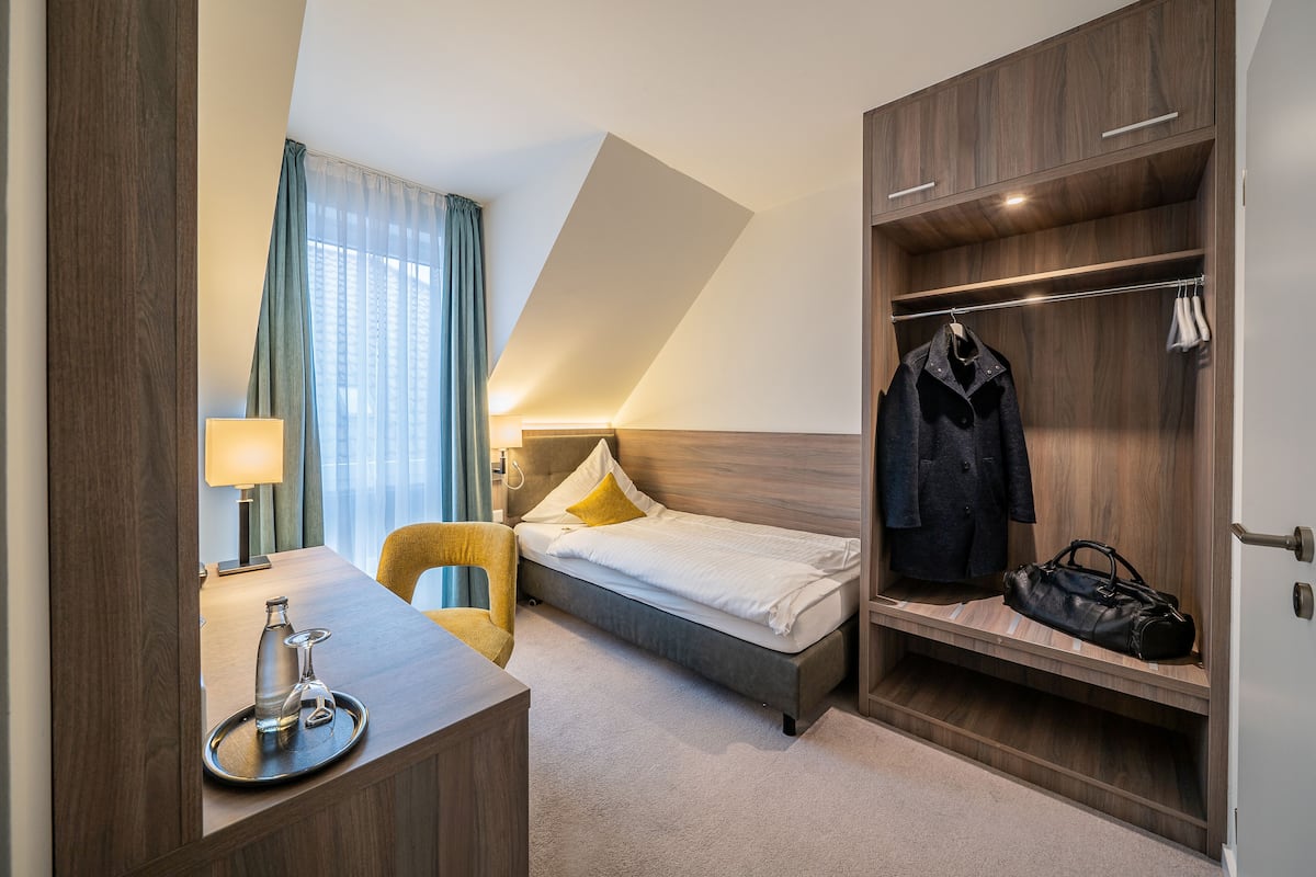 Quarto de hotel com cama, escrivaninha com luminária, cadeira, guarda-roupa e cabideiro.