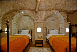 Quarto com duas camas, paredes de pedra e uma mesa de madeira.