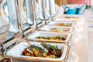 Buffet com várias estações de serviço, cada uma com uma bandeja de comida e uma tampa de metal.