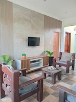 Uma sala de estar com televisão de tela plana na parede, mobiliário de madeira e piso de azulejos.
