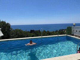 Uma piscina com água azul cristalina, cercada por vegetação e com vista panorâmica para o mar.