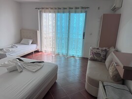 Quarto de hotel com duas camas, um sofá, um guarda-roupa e uma janela grande com cortinas.
