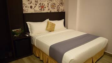 Cama bem arrumada com roupa de cama branca e bege, um travesseiro decorativo e um cobertor azul.
