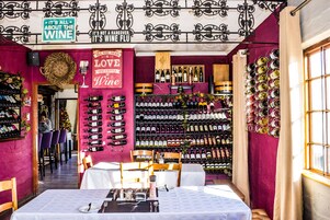 Uma loja de vinhos com diversas garrafas expostas em prateleiras e paredes, um letreiro que diz "Tudo é sobre o vinho" e uma mesa posta para refeições.