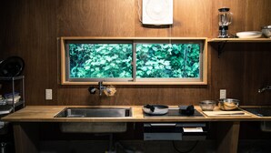 Uma cozinha com bancada de madeira, pia dupla, liquidificador e janela com vista para vegetação verde.