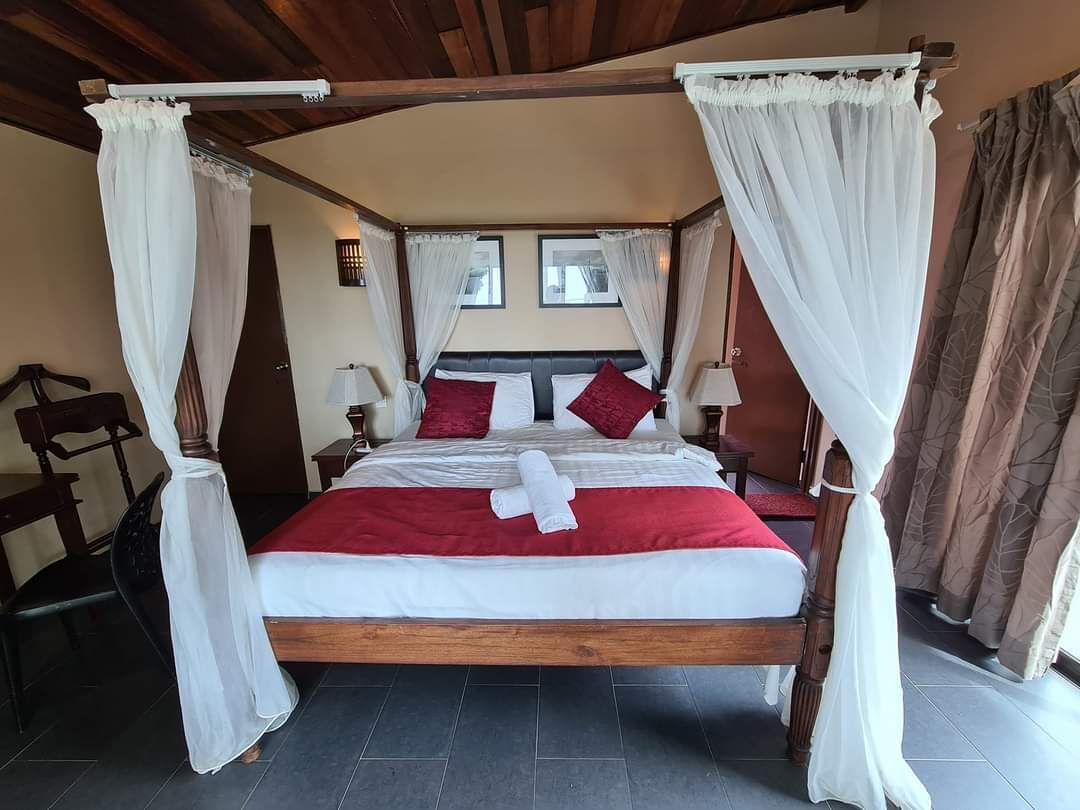 Uma cama de dossel com cortinas brancas, um cobre-leito vermelho e uma toalha branca dobrada sobre a cama.