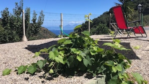 Um jardim com um caminho de cascalho, uma cadeira vermelha e vista para o mar.