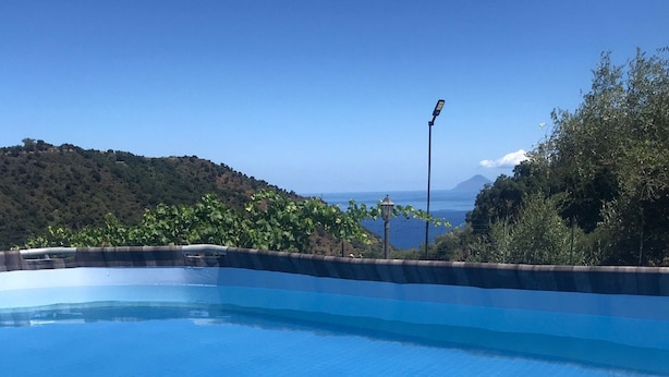 Piscina azul límpida com chão de azulejos, rodeada por vegetação e vista para colinas ao longe.