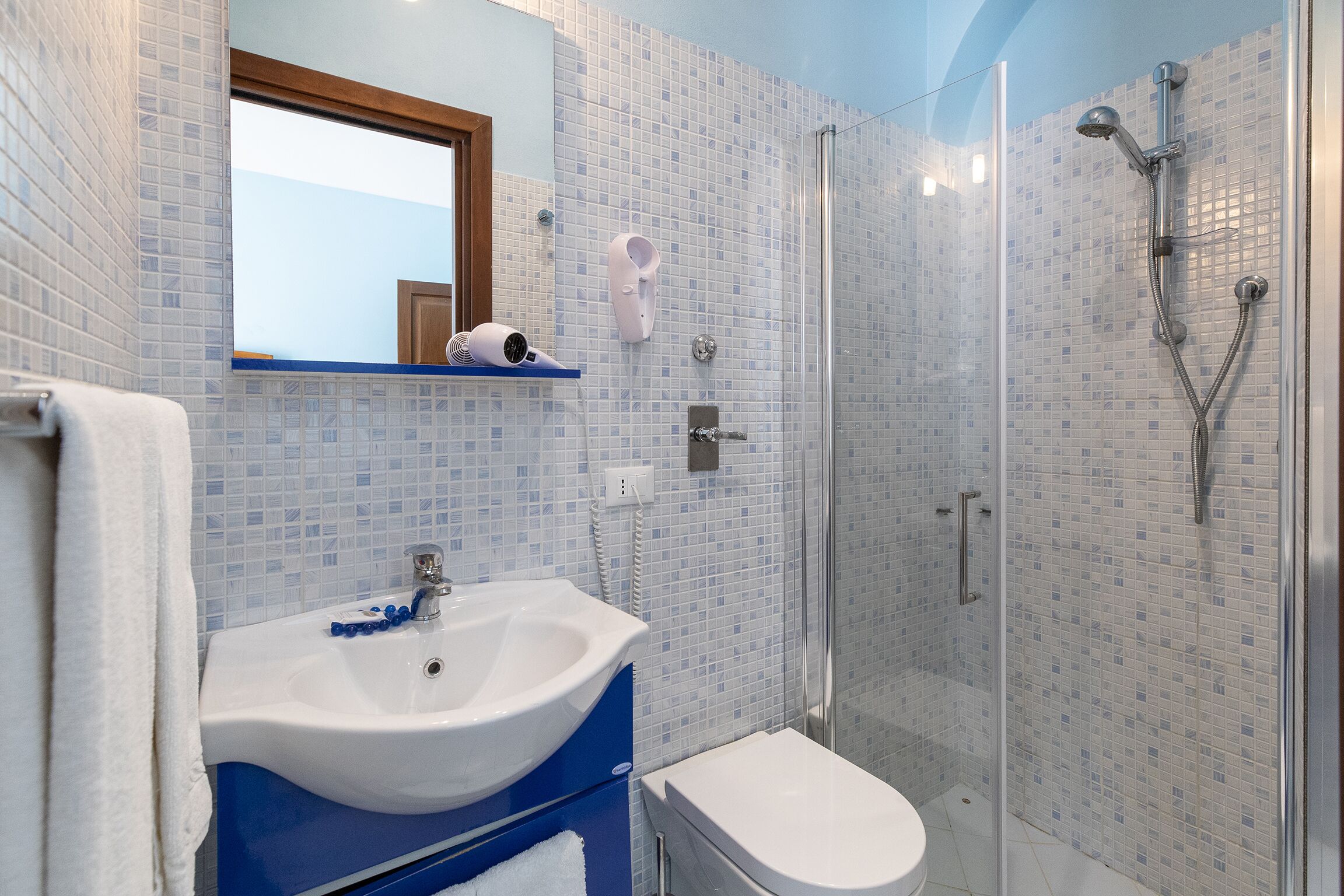 Casa de banho com lavatório branco, armário azul e cabine de duche em vidro.