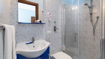 Casa de banho com lavatório branco, armário azul e cabine de duche em vidro.