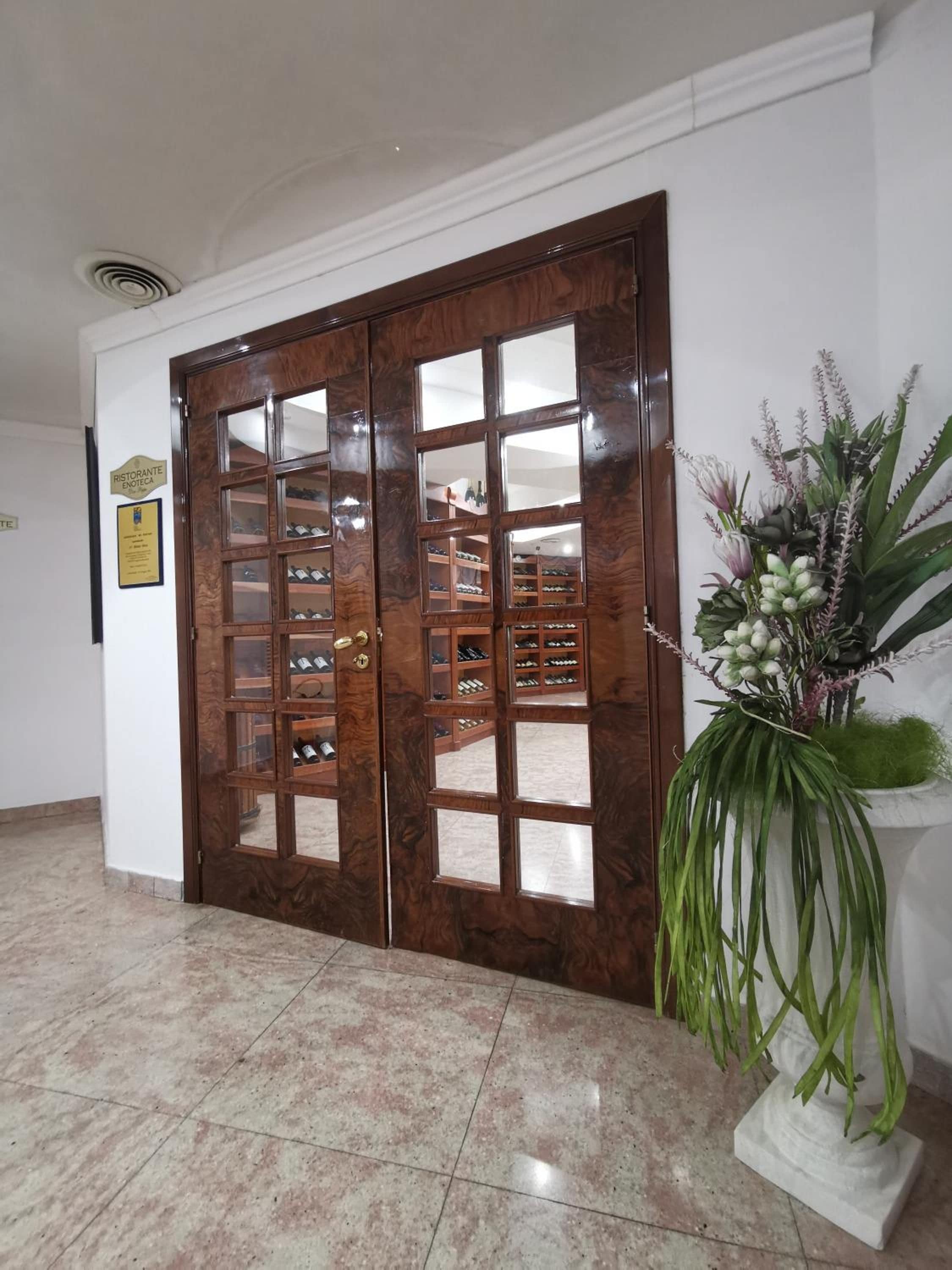 Uma porta dupla de madeira com painéis de vidro, dando acesso a uma área de exposição de sapatos.