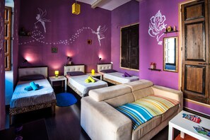 Quarto com três camas, um sofá e paredes roxas com ilustrações de fadas e elefantes.