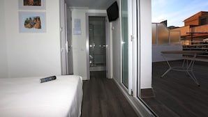 Quarto de hotel com cama, televisão na parede e varanda com mesa e cadeiras.