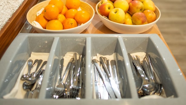 Buffet com tigelas de laranjas, maçãs e bananas, e uma vitrine ao fundo.