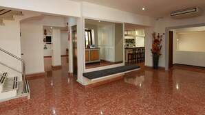 Um interior espaçoso com piso de mármore vermelho polido, uma escadaria com grades de metal e uma área de cozinha visível através de uma porta aberta.