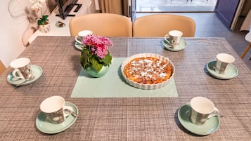 Uma mesa de jantar posta com uma torta, xícaras, pires e um vaso de flores.