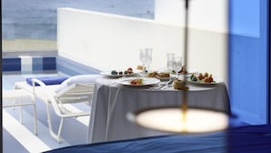 Mesa de jantar posta com pratos, copos e talheres numa varanda com vista para o mar.