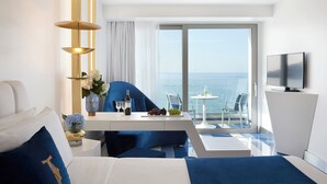 Quarto de hotel moderno com uma cama, uma escrivaninha com um vaso de flores, uma cadeira, uma TV e uma varanda com vista para o mar.
