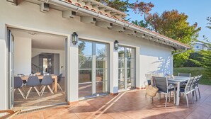 Uma casa moderna com um pátio, portas de correr e uma área de refeições com mobiliário de exterior.