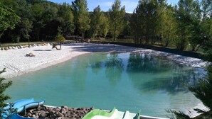 Uma piscina ao ar livre cristalina rodeada por árvores, com dois toboáguas a descer para a água.