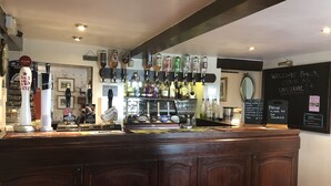 Uma área de bar com balcão de madeira, diversas torneiras de cerveja e um cardápio em lousa.