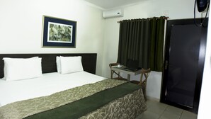 Quarto de hotel com cama, escrivaninha com laptop, quadro na parede e porta com cortinas.