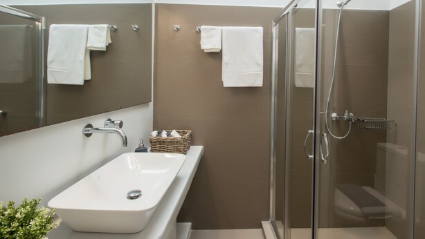 Uma casa de banho moderna com chuveiro de vidro, lavatório branco e um espelho grande.