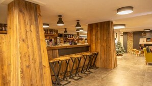 Uma área de bar com banquetas de madeira e balcão, cercada por painéis de madeira e iluminação pendente.