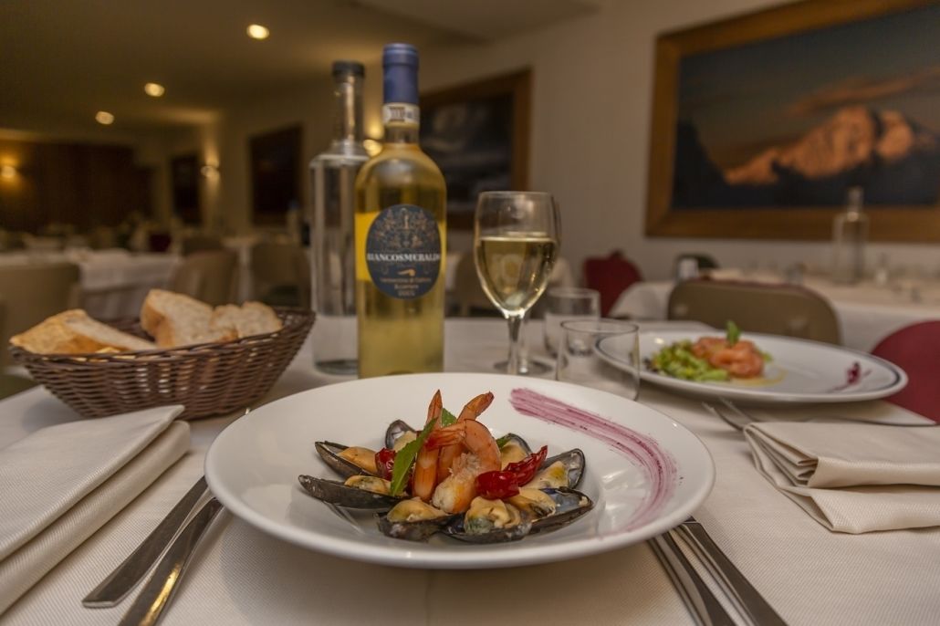 Uma mesa de jantar com pratos de frutos do mar, uma garrafa de vinho e um copo de vinho branco.