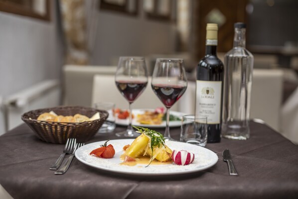 Uma mesa de jantar com um prato de comida, duas taças de vinho, uma garrafa de vinho e uma cesta de pão.