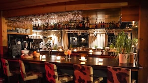 Uma área de bar com balcão de madeira, várias garrafas de vinho, copos e um vaso com planta.