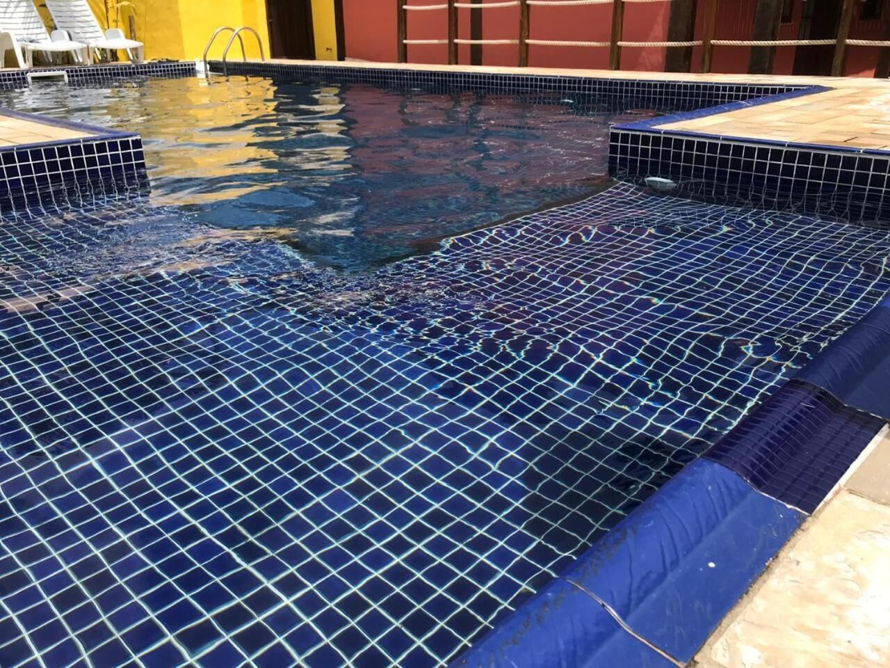 Piscina com azulejos de mosaico azul e área de deck de madeira.