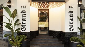 Entrada de hotel com design moderno, destacando uma escadaria que leva ao saguão e grandes vasos de plantas na entrada.